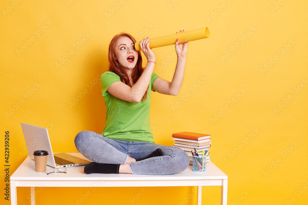 Astonished red haired student female looking through twisting paper ...