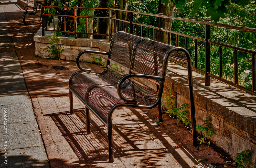 Modern tubular and mesh metal formed bench sits in the sunshine on an ...