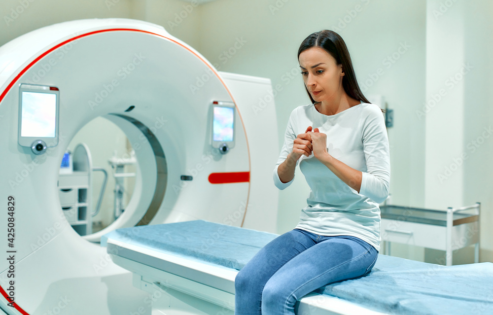 An agitated, sad and frightened patient sits on the bed of a CT or MRI ...