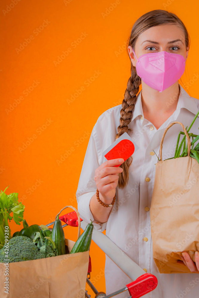Attractive young lady wearing an pink CORONAVIRUS MASK (COVID19) close to a shopping cart having ...