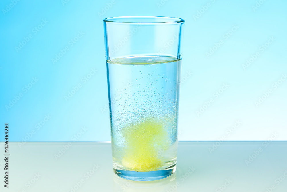 yellow dissolving pill dissolves in water on colored background. a ...
