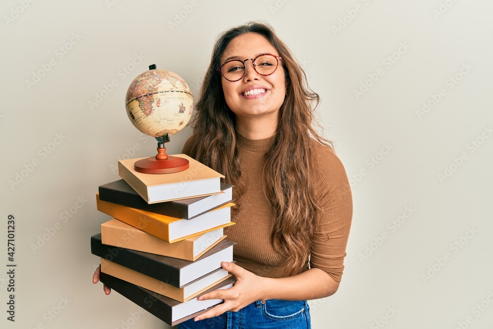 Foto de Stock Young hispanic girl studying geography smiling with a happy and cool smile on face ...