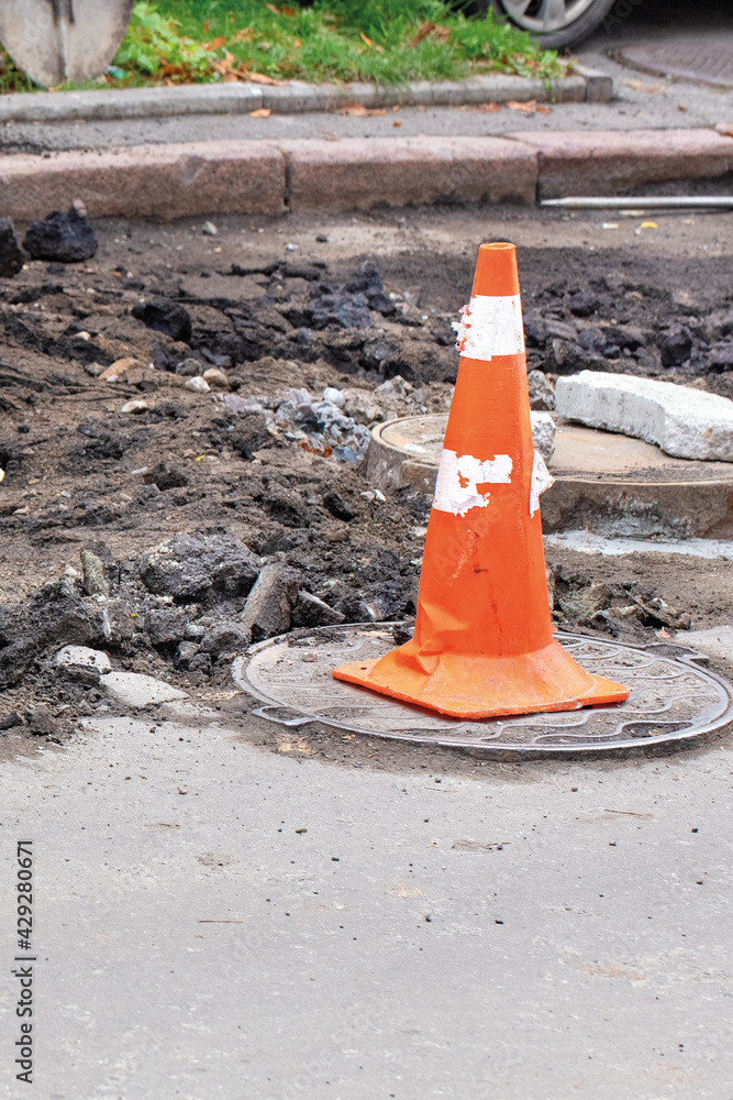 An orange traffic cone stands on the manhole and encloses the danger ...