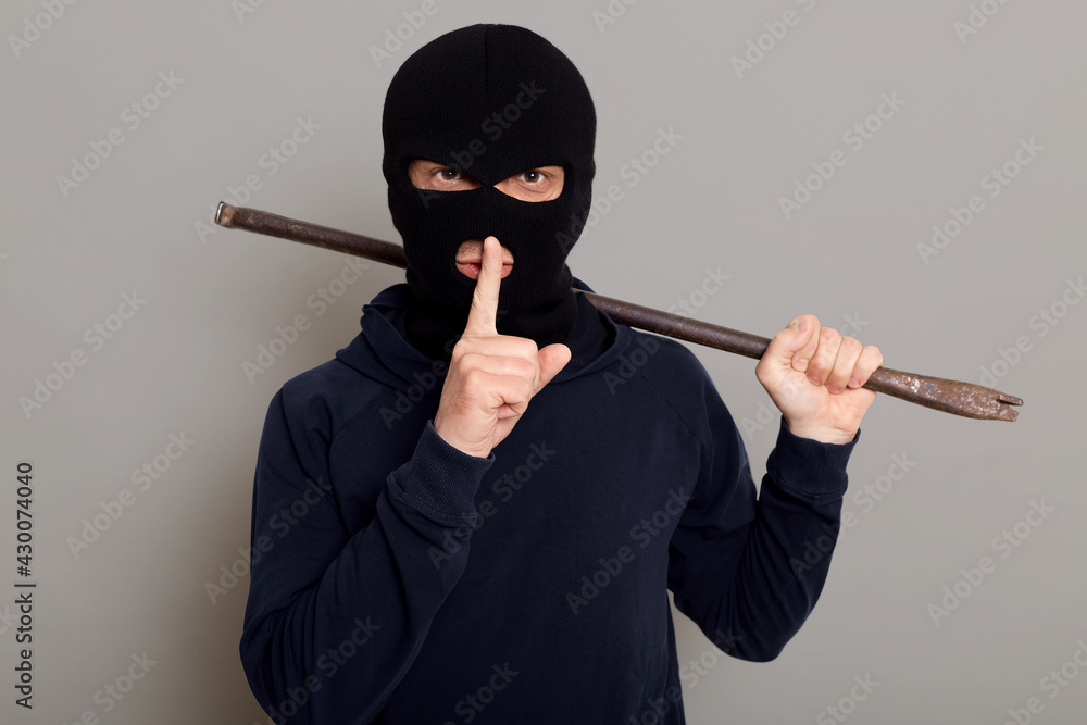 Young guy robber man dressed in a black hoodie with masked face, holds ...