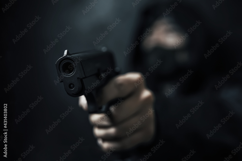 Masked robber with gun aiming into camera. Man in hood threatens with ...