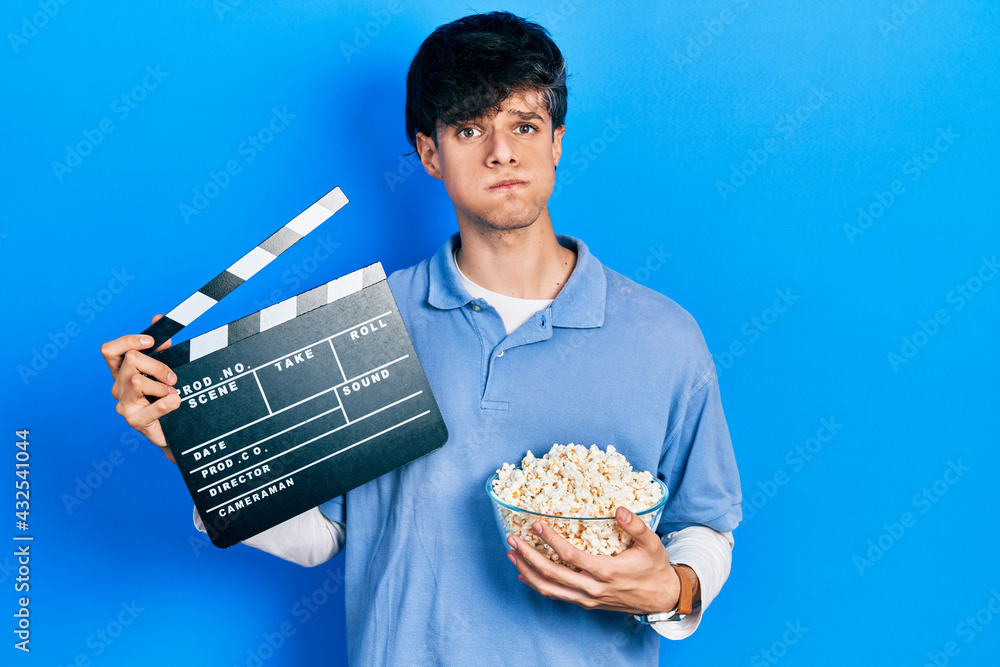 Handsome hipster young man eating popcorn holding cinema clapboard ...