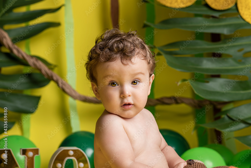 Niño caucásico de un año en fondo amarillo con hojas grandes y globos ...