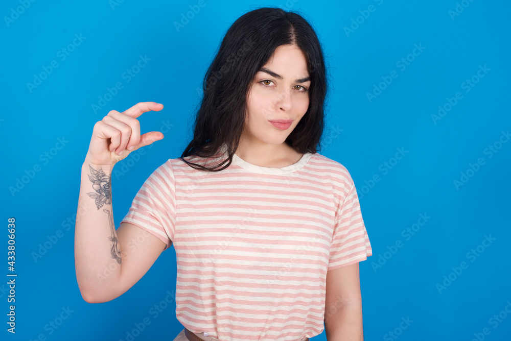 Displeased young beautiful tattooed girl wearing pink striped t-shirt ...