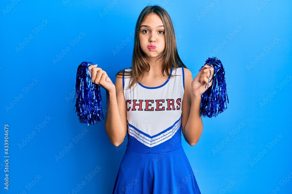 Young brunette woman wearing cheerleader uniform puffing cheeks with ...