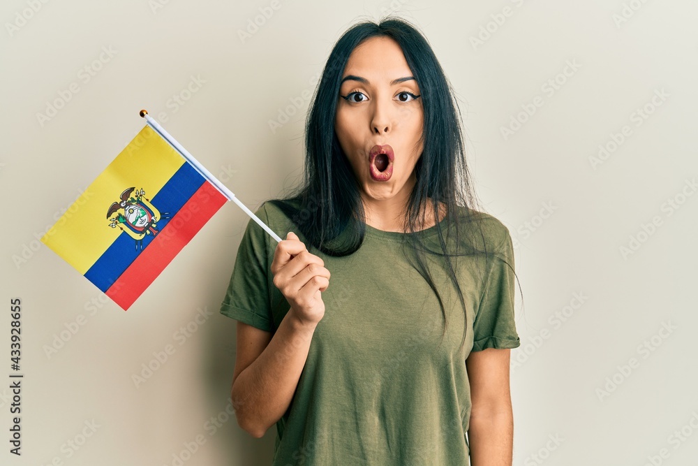 Young hispanic girl holding ecuador flag scared and amazed with open ...