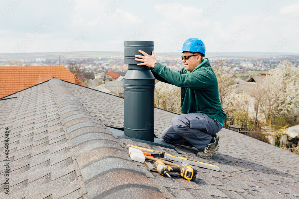 worker with blue helmet on the roof installing iron chimney. roofing ...