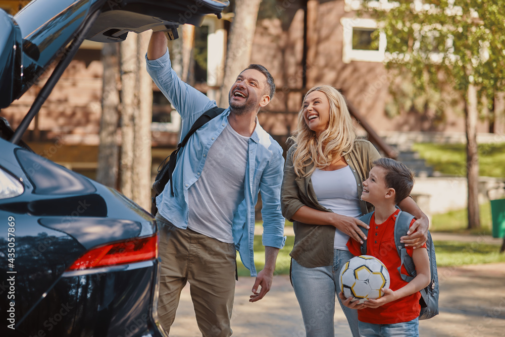 Happy family with little boy packing stuff into the car while standing ...