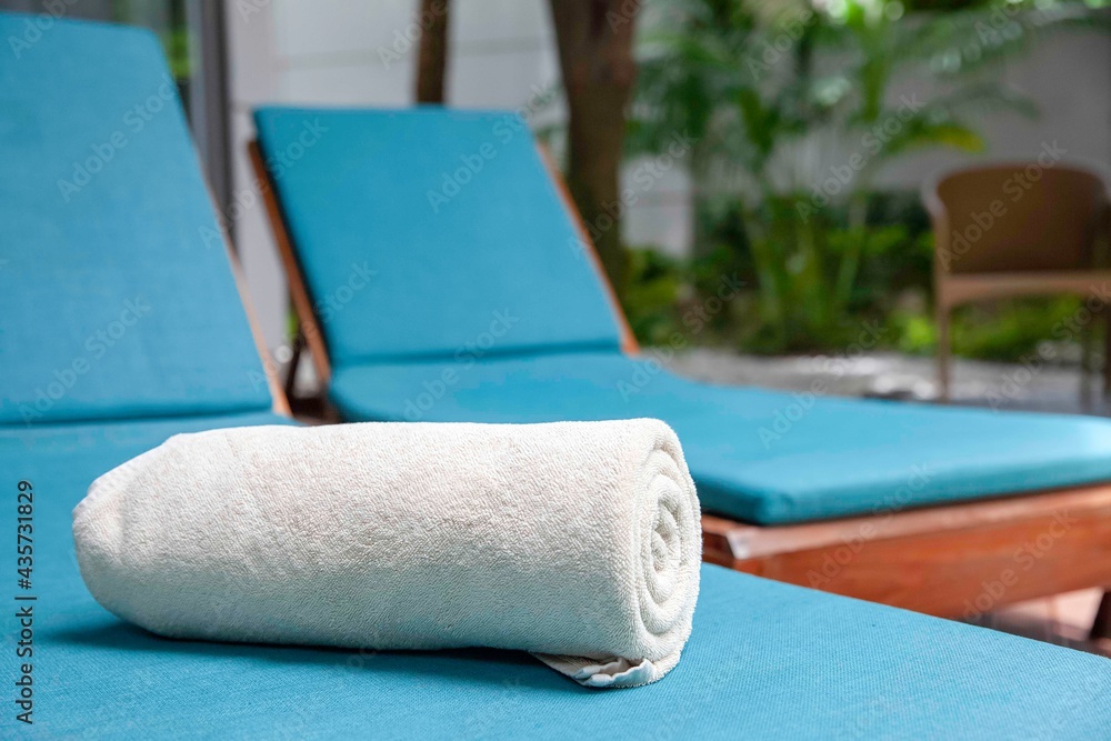 Brown pool towels are rolled up and placed on a sunbed by the pool in a ...