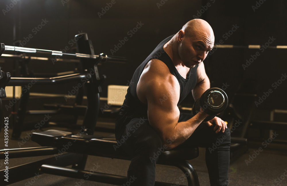 Muscular man working out in gym doing exercises with dumbbells at biceps, strong male naked ...