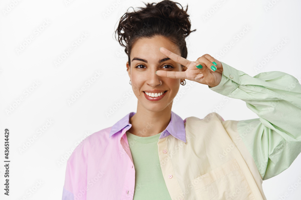 Positive brunette girl shows peace v-sign and smiles happy, standing ...