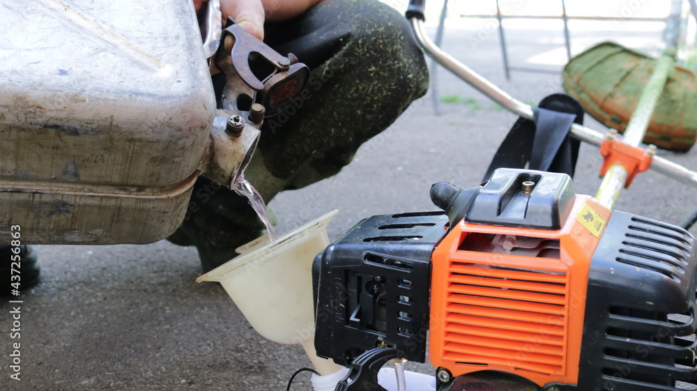 hands of a worker pouring gasoline into a lawn mower tank from an iron ...