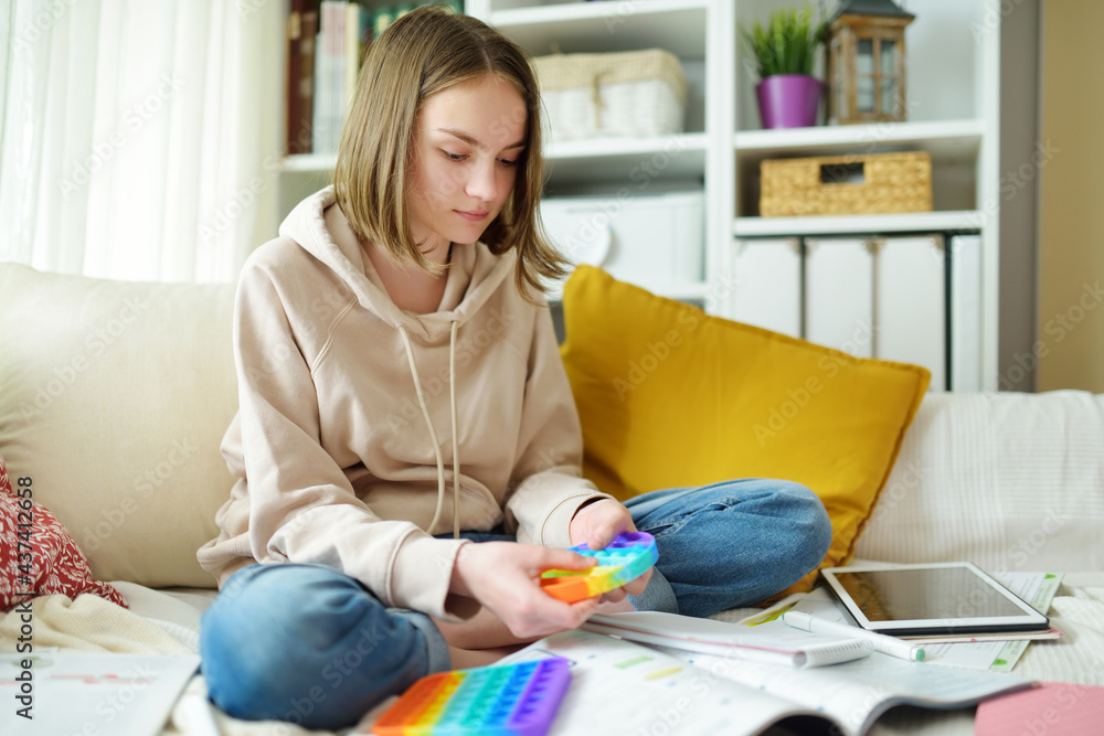 Teenage girl playing with rainbow pop-it fidget toy while studying at ...