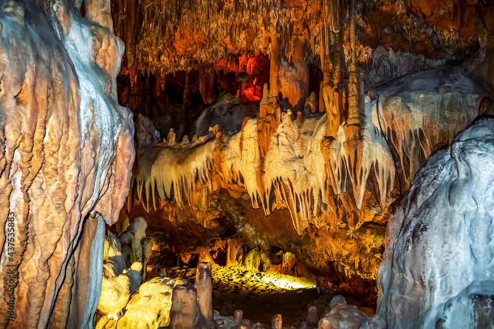 Stalactites and stalagmites illuminated with yellow-orange light inside ...