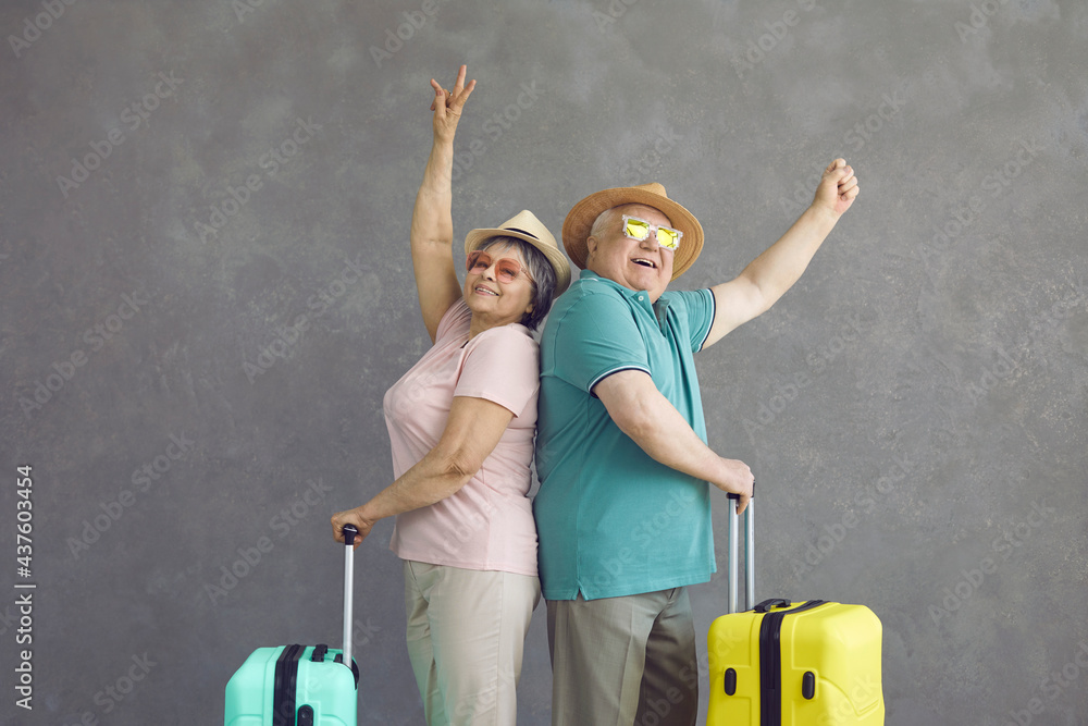 Portrait of smiling married senior couple with suitcases standing back ...