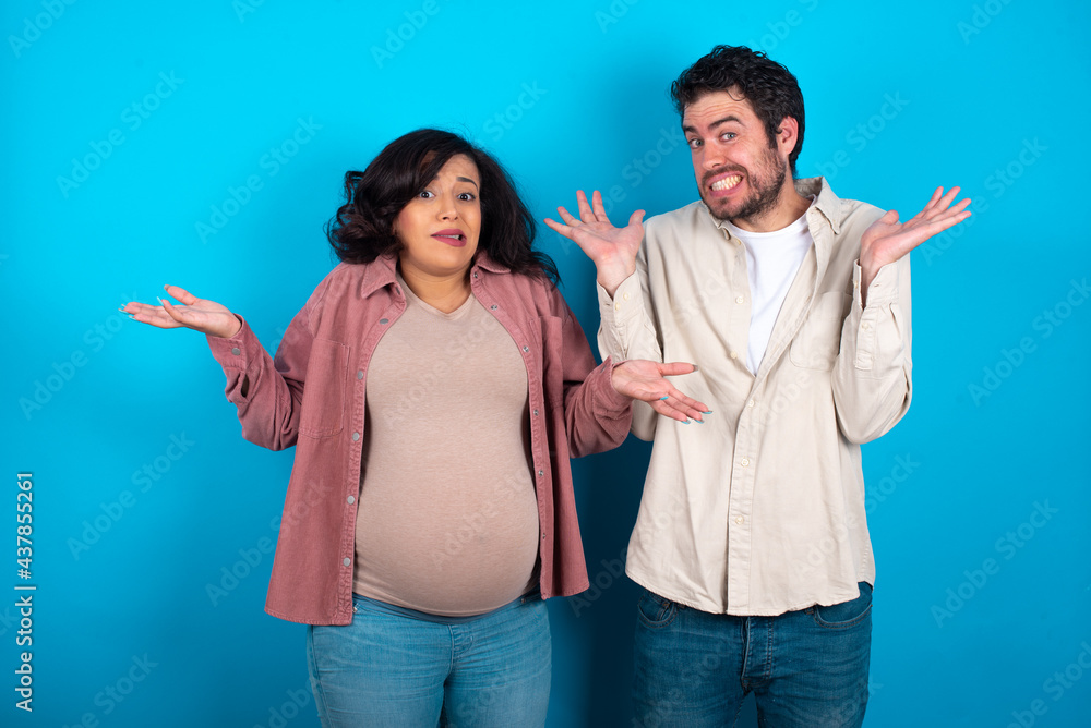 Clueless young couple expecting a baby standing against blue background ...