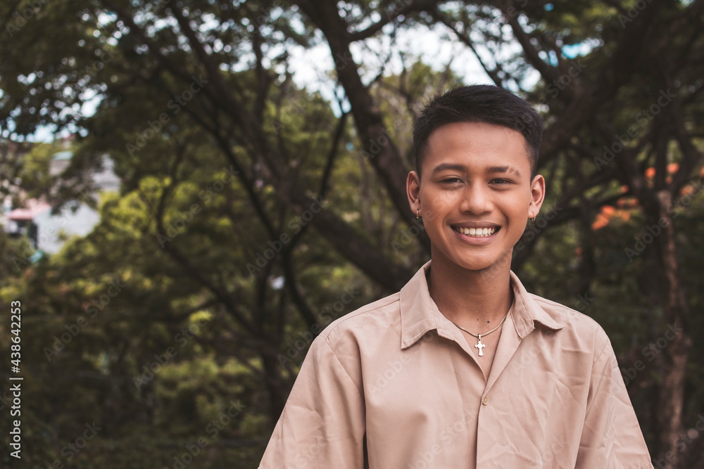A young smiling Filipino man at the park. Dark complexion and wearing a ...