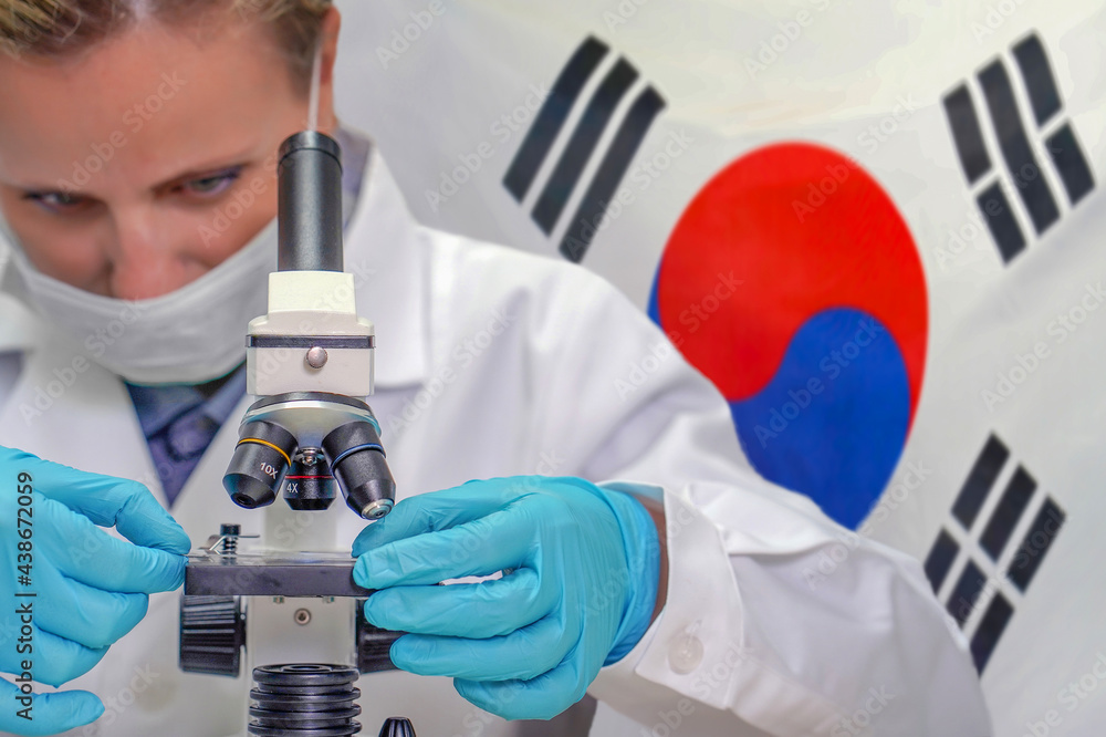 Female biochemist looking through a microscope against South Korea flag ...