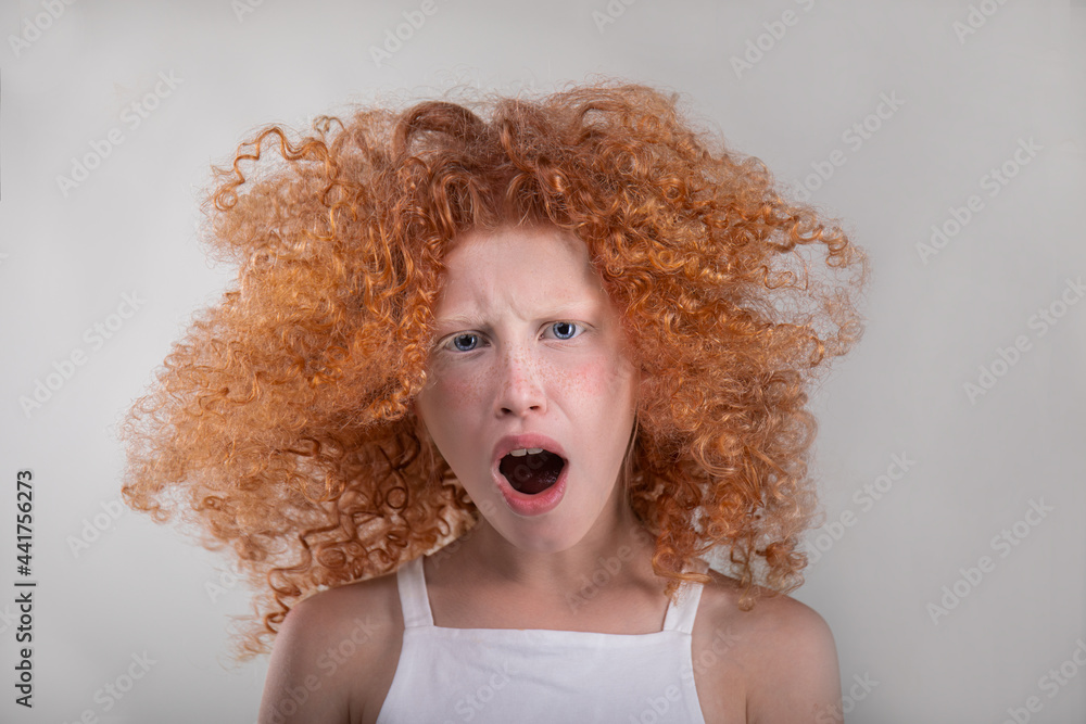 Red-haired curly girl screams from indignation with an open mouth and ...