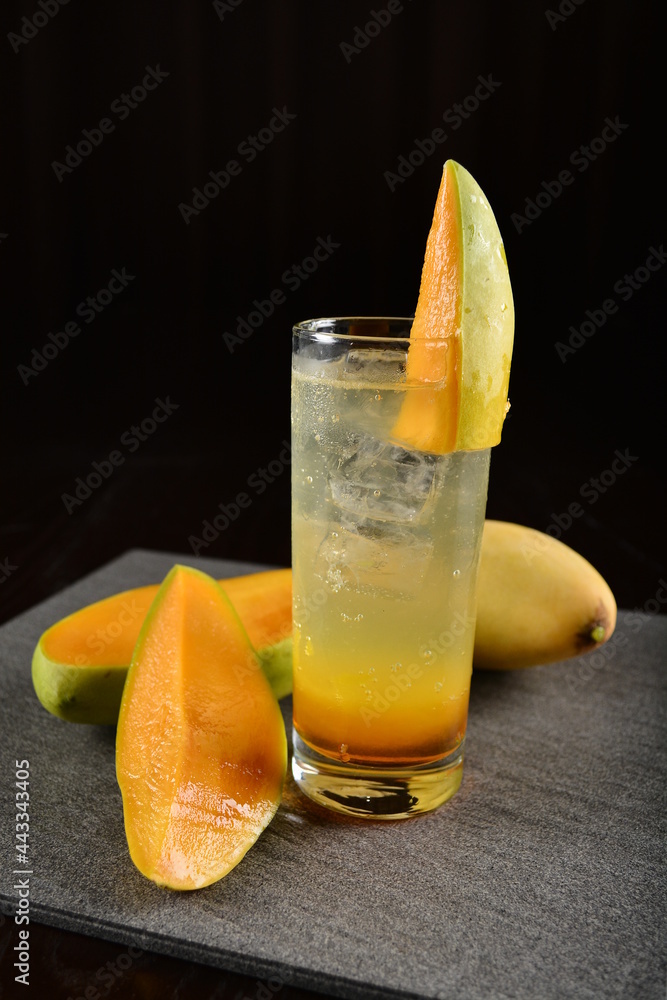 iced Thai mango fruit mocktail with soda kombucha in glass on bar counter dark night background ...