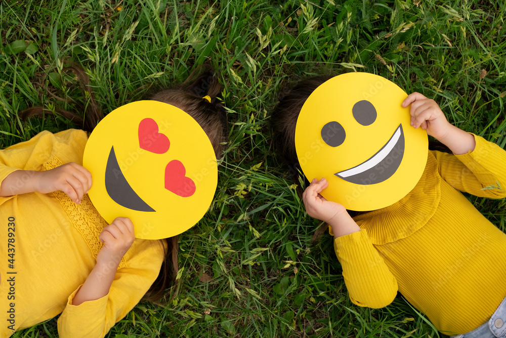 Two children hide behind the faces of cardboard funny happy emoticons ...