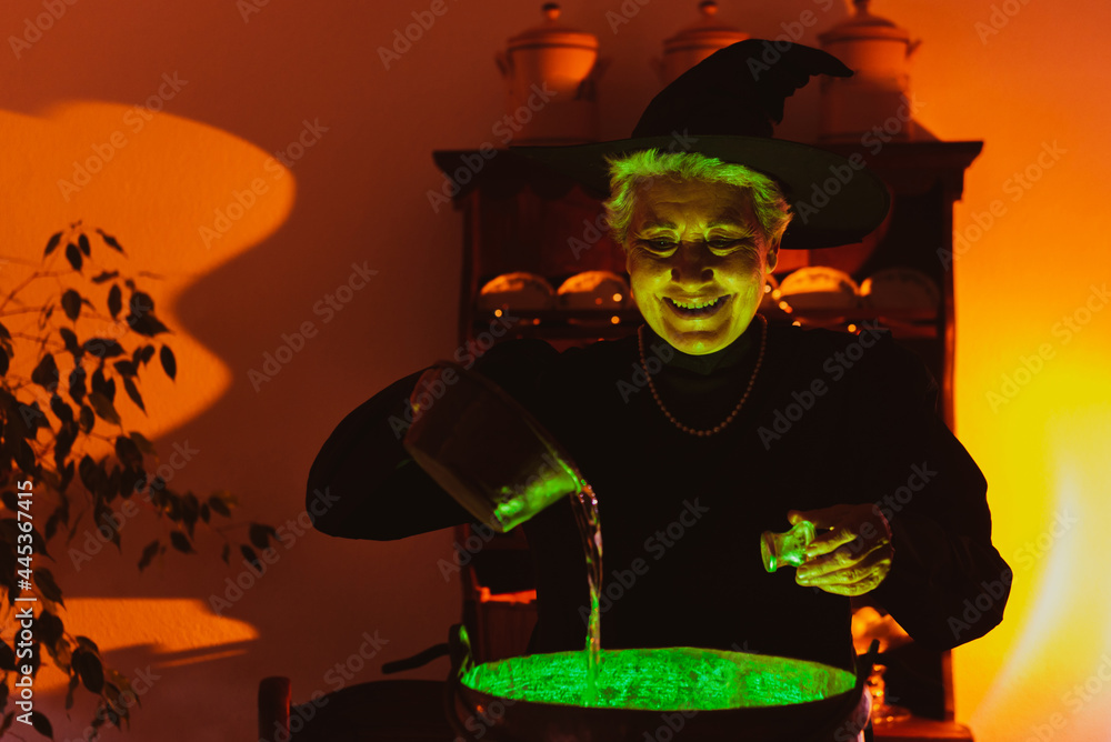 Older woman disguised as a classic witch with a malefic smile preparing ...