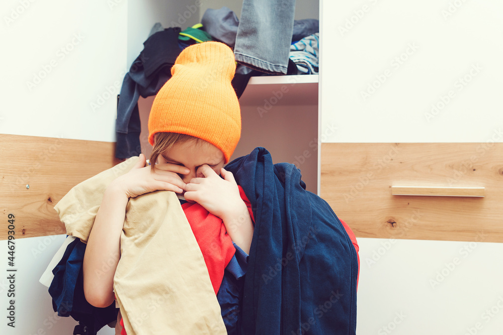 Tired stressed boy cleaning his wardrobe. Boy holding pile of dirty ...