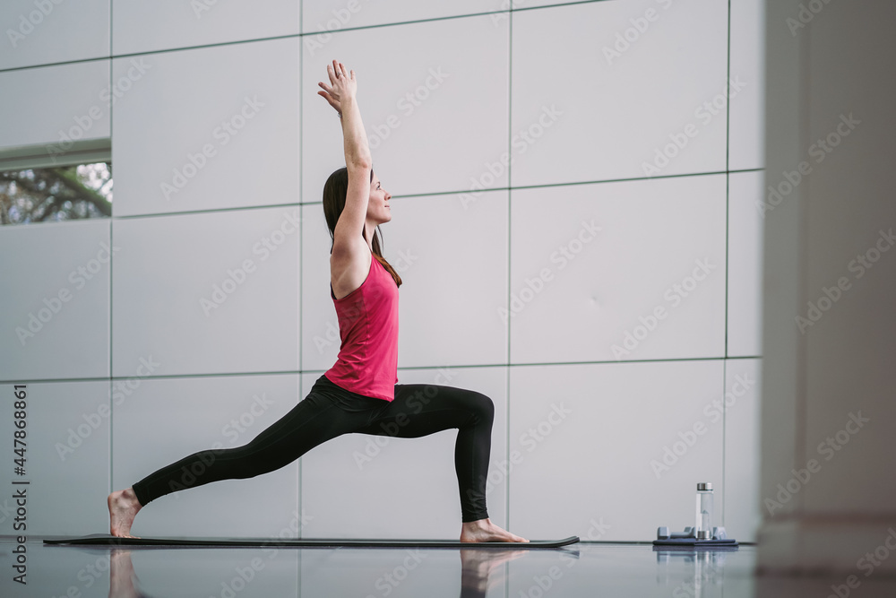 trained brunette woman in black leggin stretching slim body while practicing warrior 2 yoga pose ...