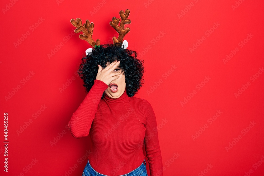 Young middle east woman wearing cute christmas reindeer horns peeking ...