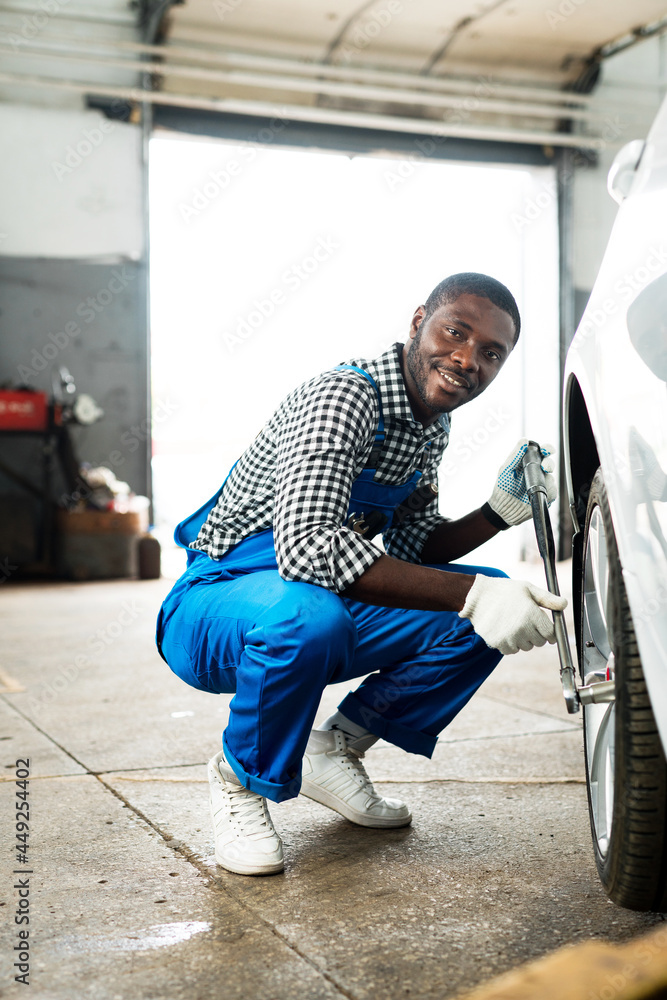 Happy african mechanic with ratchet wrench repairing tire in white ...