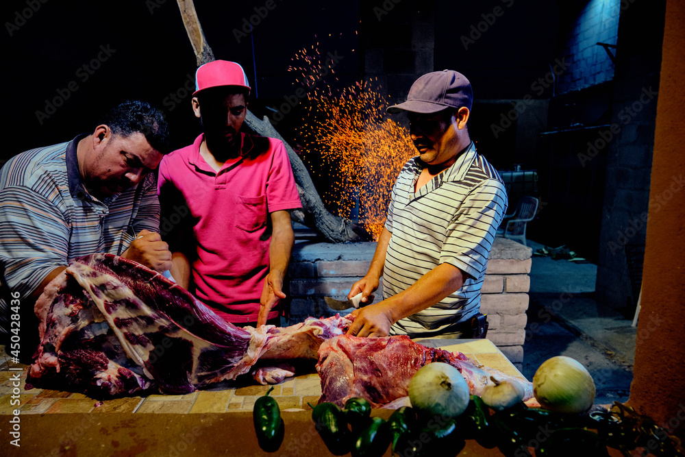 Dad, son and uncle preparing meat for a Mexican style barbecue on a pit ...
