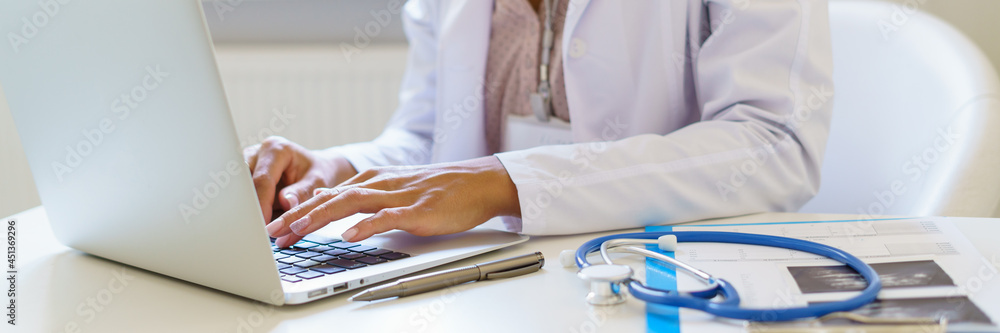 Cropped photo of female doctor in white uniform working on laptop ...