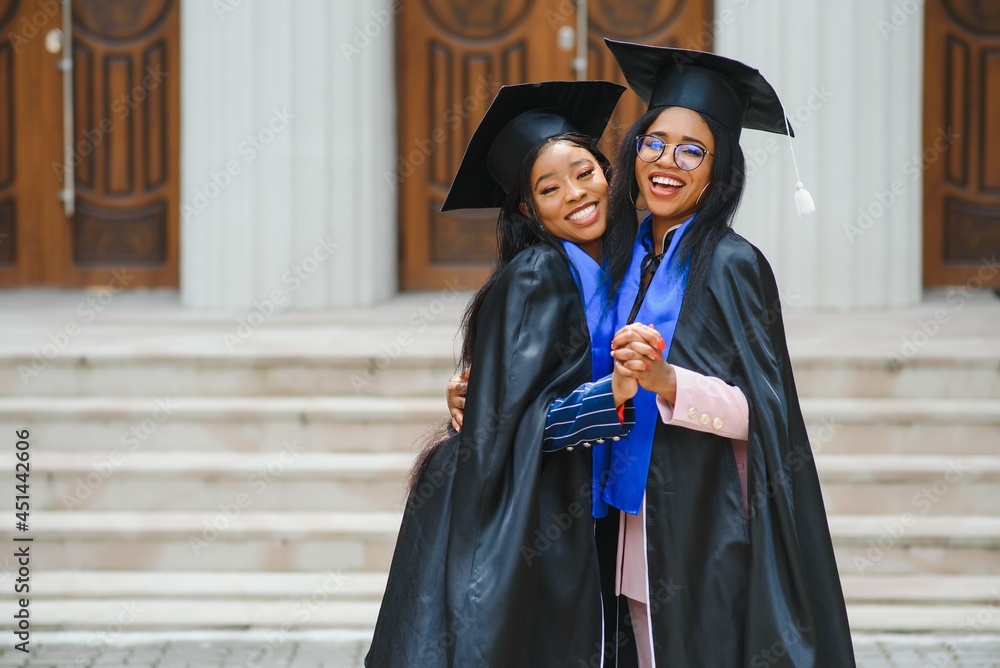 two young ladies in graduation costumes posing at camera at university ...