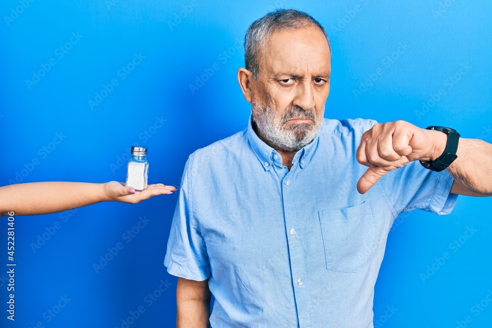 Handsome senior man with beard being offering salt with angry face ...