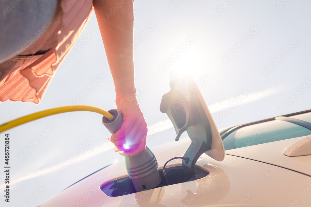 Female hands opening an electric car charging socket cap and plugging ...