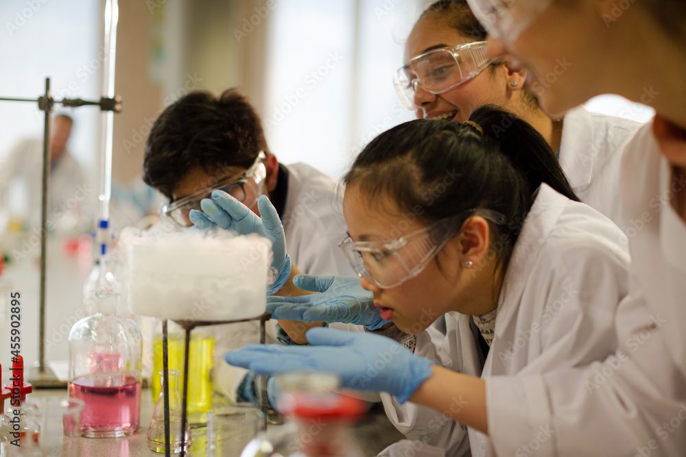 Female teacher and students watching scientific experiment chemical ...