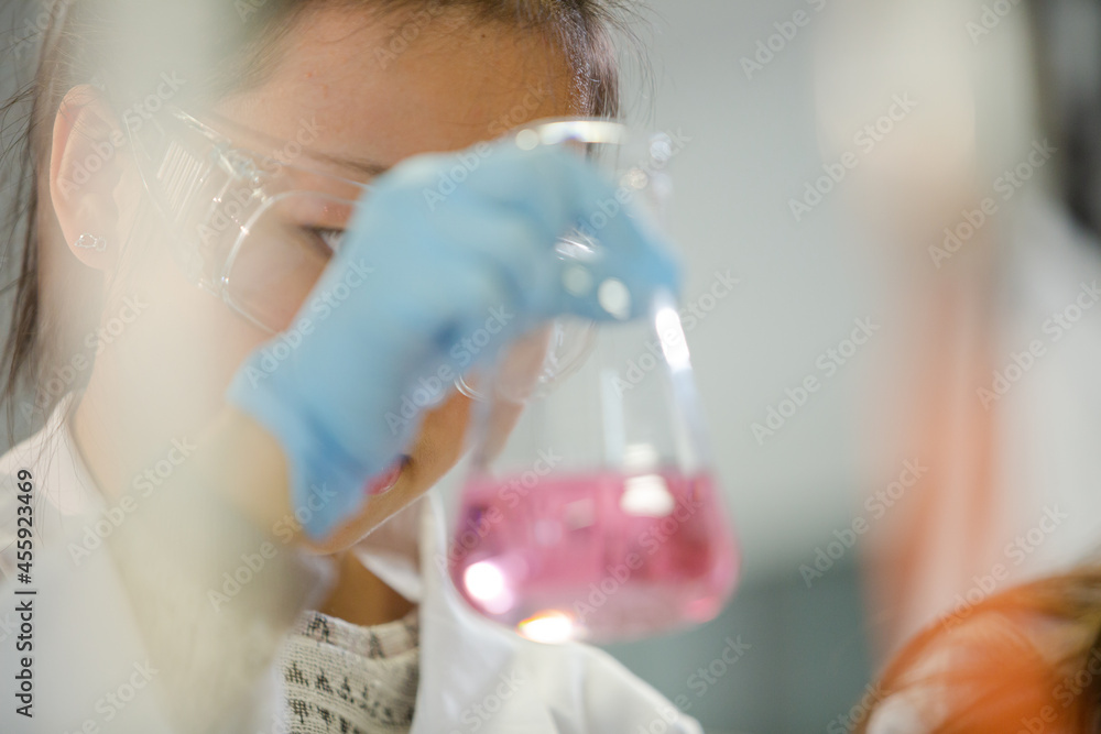 Girl student examining pink liquid, conducting scientific experiment in ...