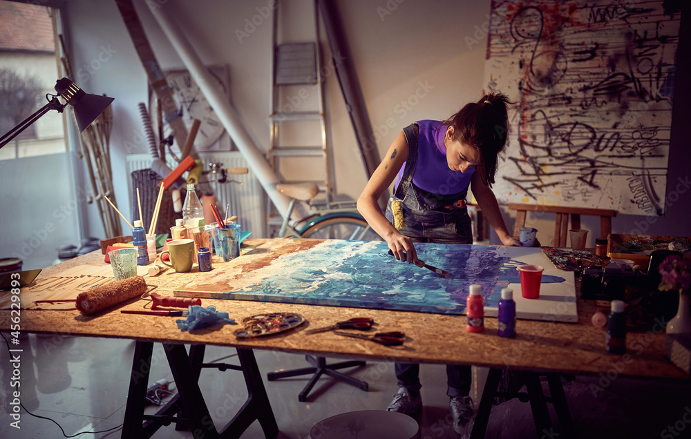 A young female artist is focused while working on a painting in the ...