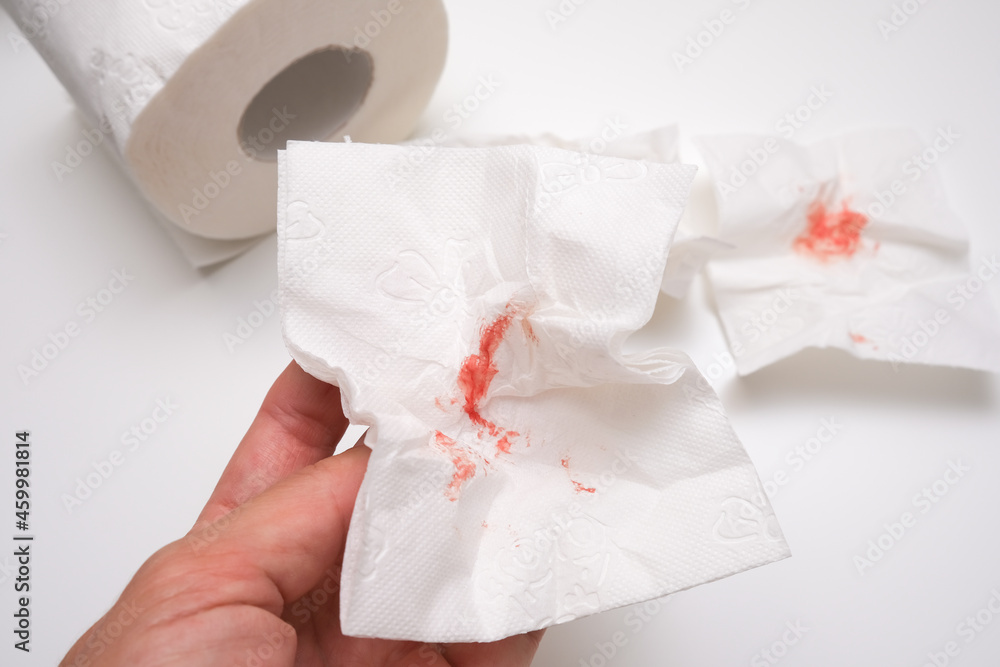 Hand holding used sheet of bloody toilet paper and a roll on white ...