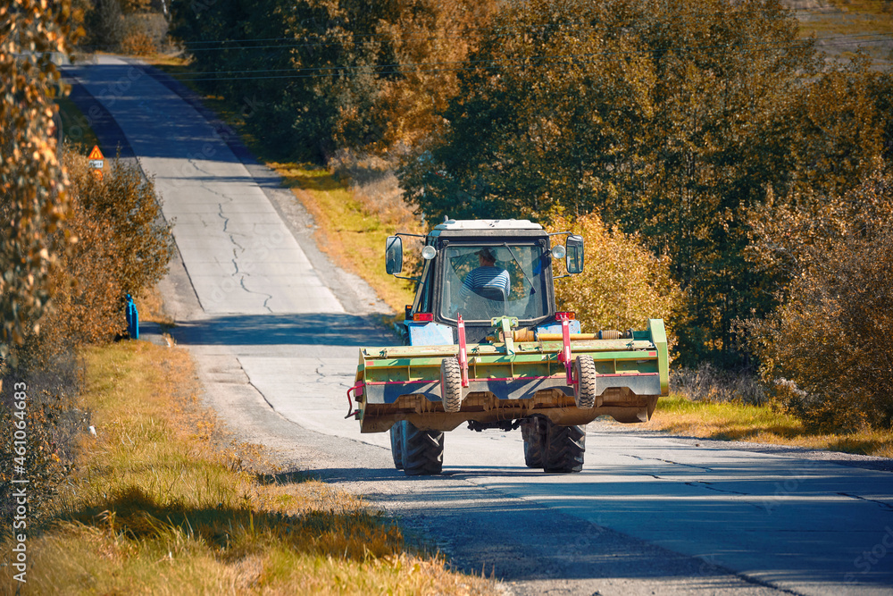 Tractor with plough rides along rural asphalt road. Tractor and rolling ...