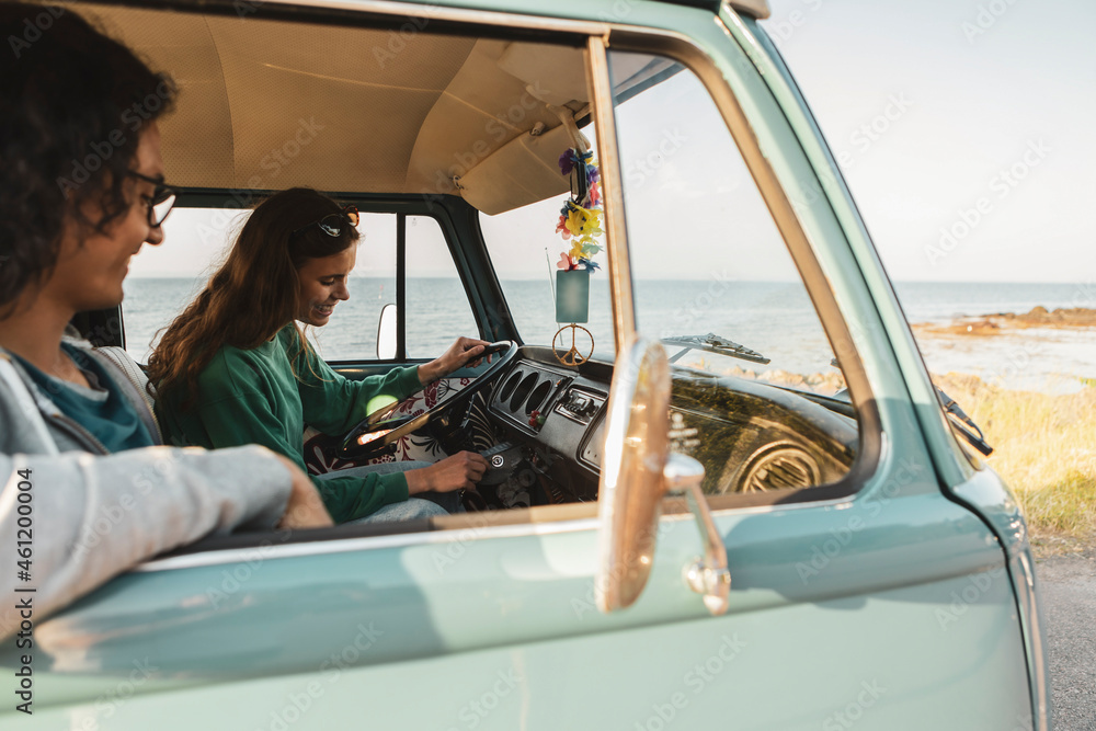 Woman starting engine of camping van sitting by male friend during road ...