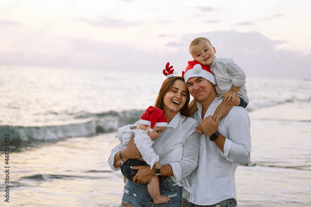 Family in a red Santa hat walk on the beach. Family celebrate Christmas ...