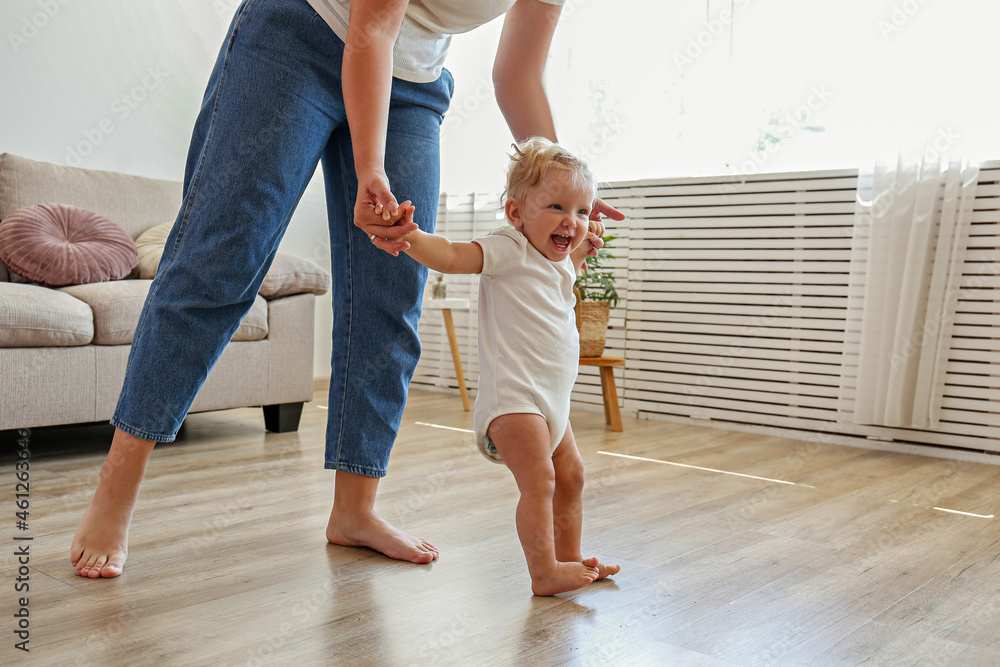 First steps of a little girl. A blond toddler learning to walk at home ...