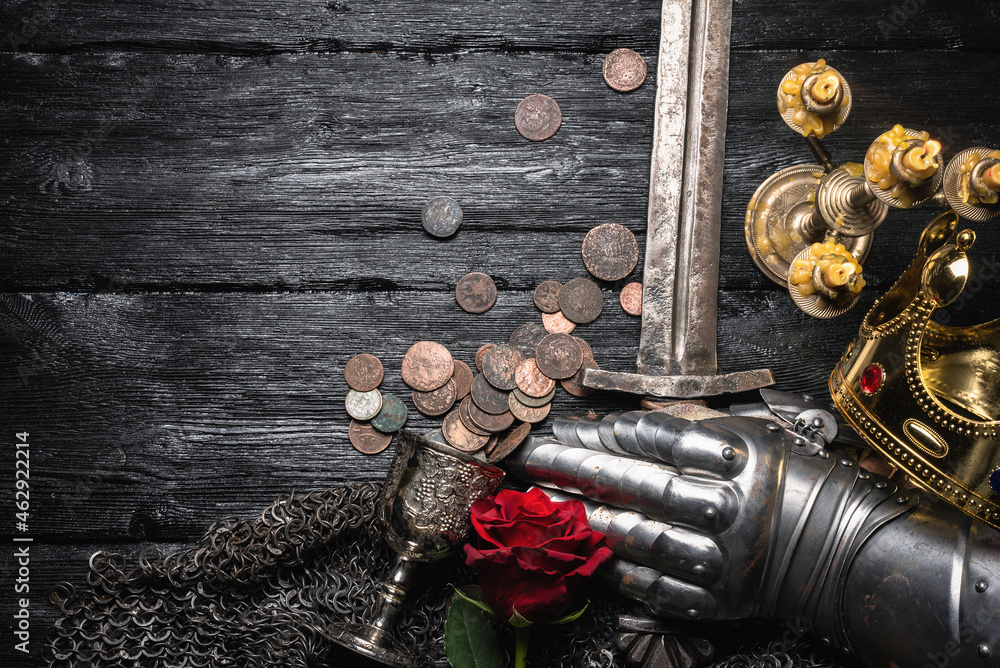 Knight sword, golden crown and red rose flower on the black woorden ...