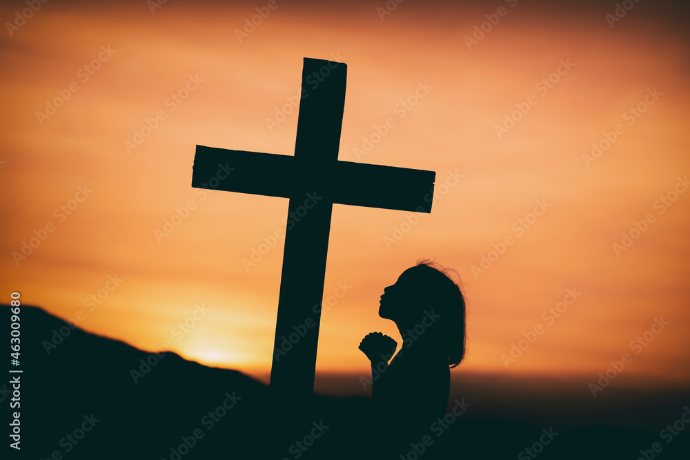 young girl standing praying under the cross with light of sunset ...