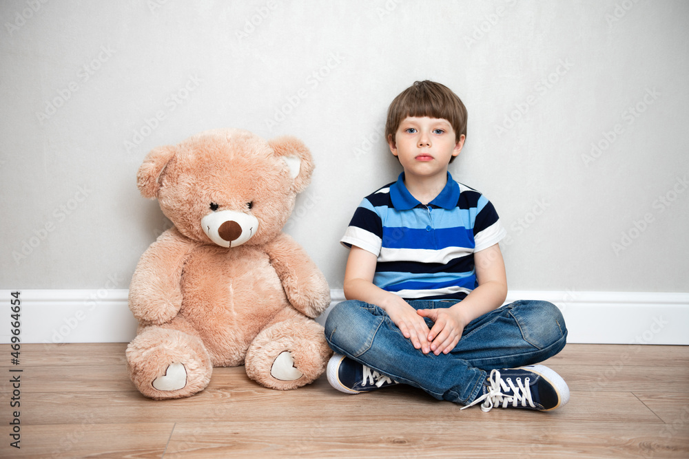 Sad little boy with a big teddy bear is sitting at home. Loneliness and ...